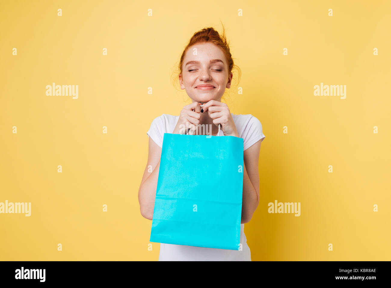 Pleased ginger woman holding packet in hands with closed eyes over ...