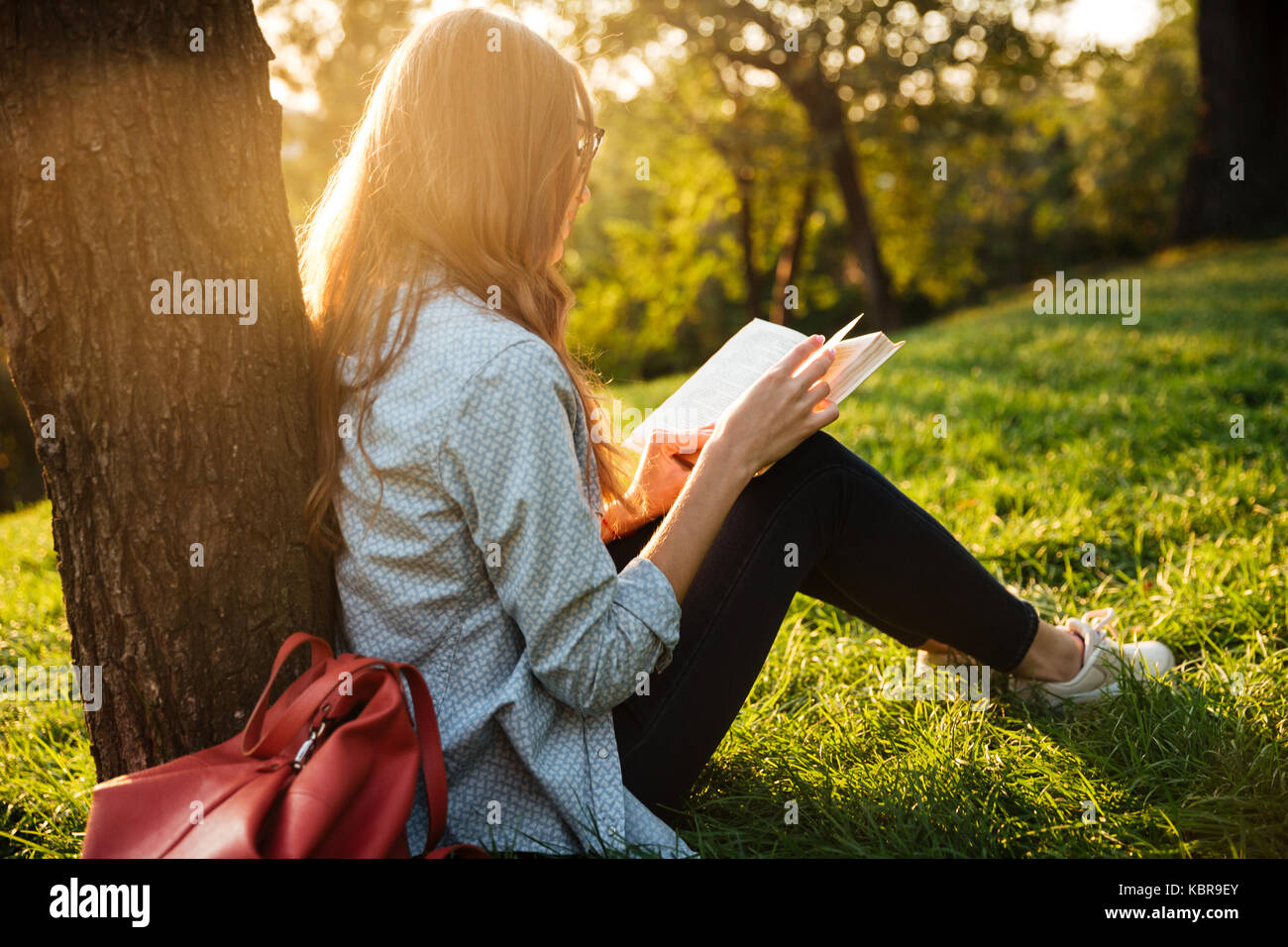 Side view of pretty brunette woman sitting near the tree in park and ...