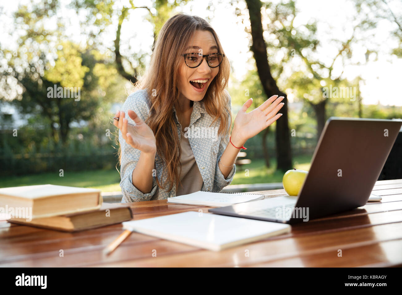 Happy shocked woman in eyeglasses sitting by the table in park with ...