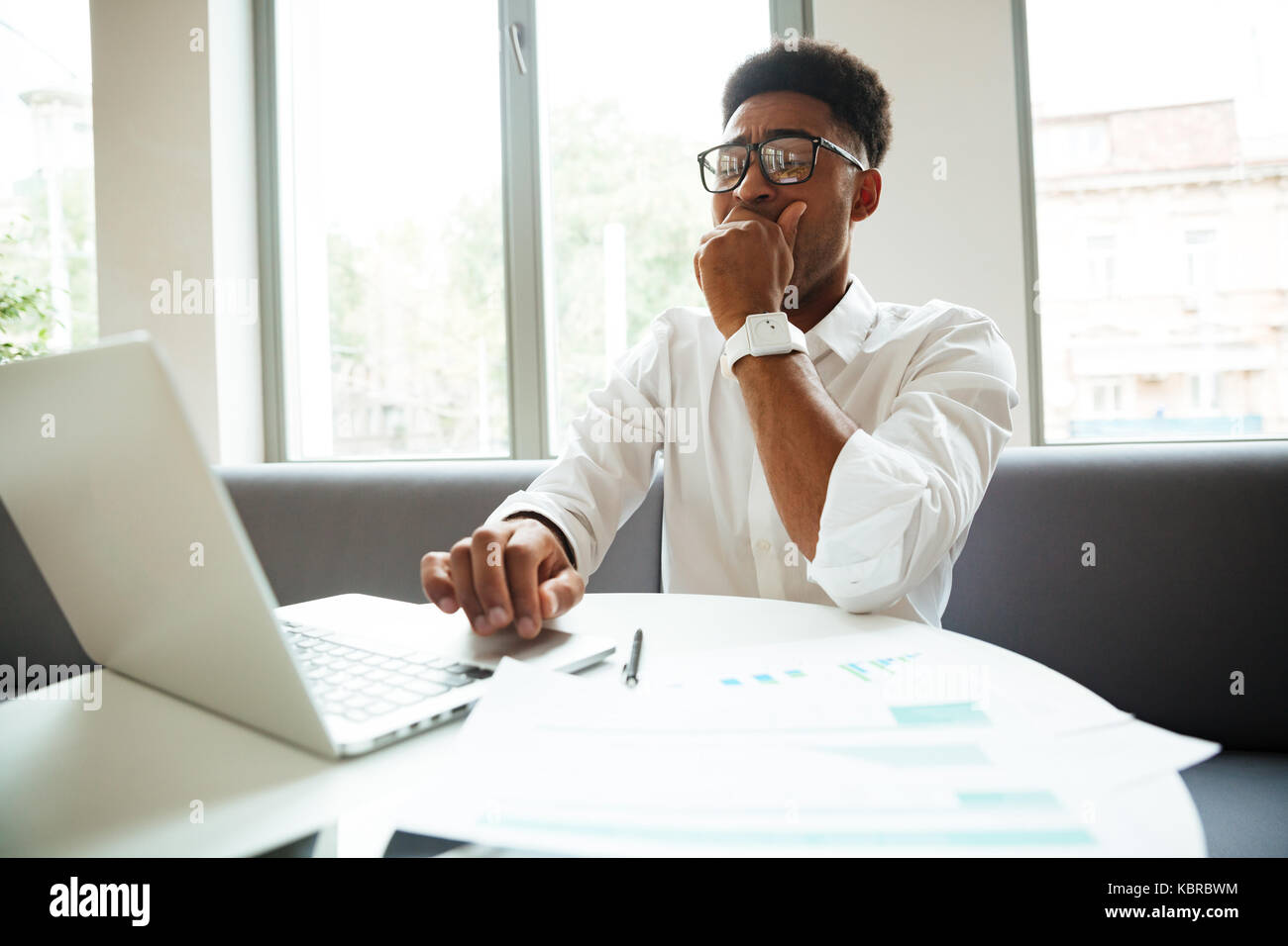 Image of yawning young african man sitting coworking by laptop computer ...
