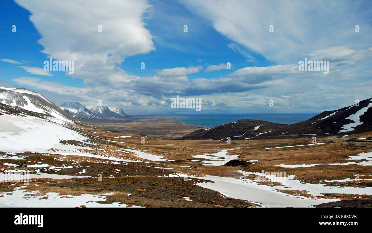 A landscape view of a wide valley between hills with snow capped ...