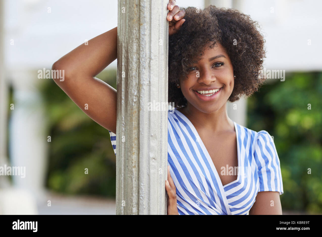 Portrait of pretty afro american woman standing behind column smiling ...