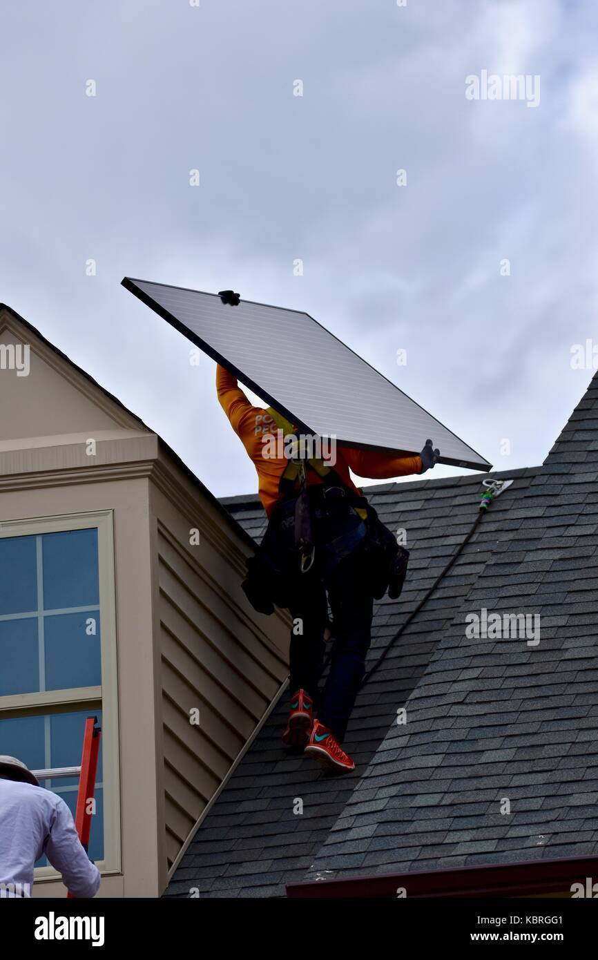 Solar panel technician carrying solar panels up ladder onto the roof of ...