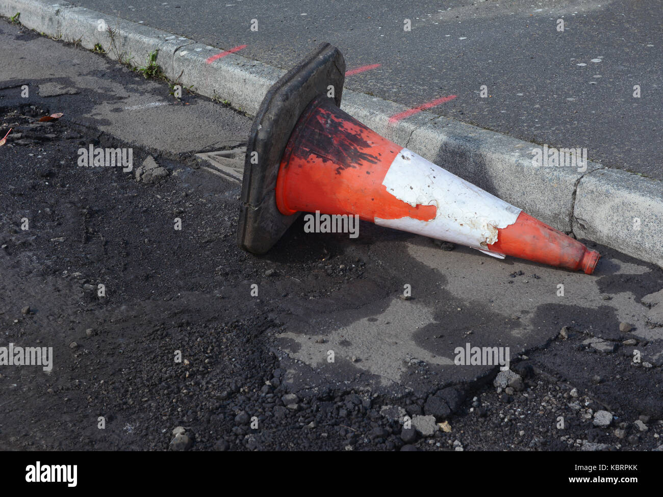 Orange and white damaged traffic cone lying in the gutter. The road ...