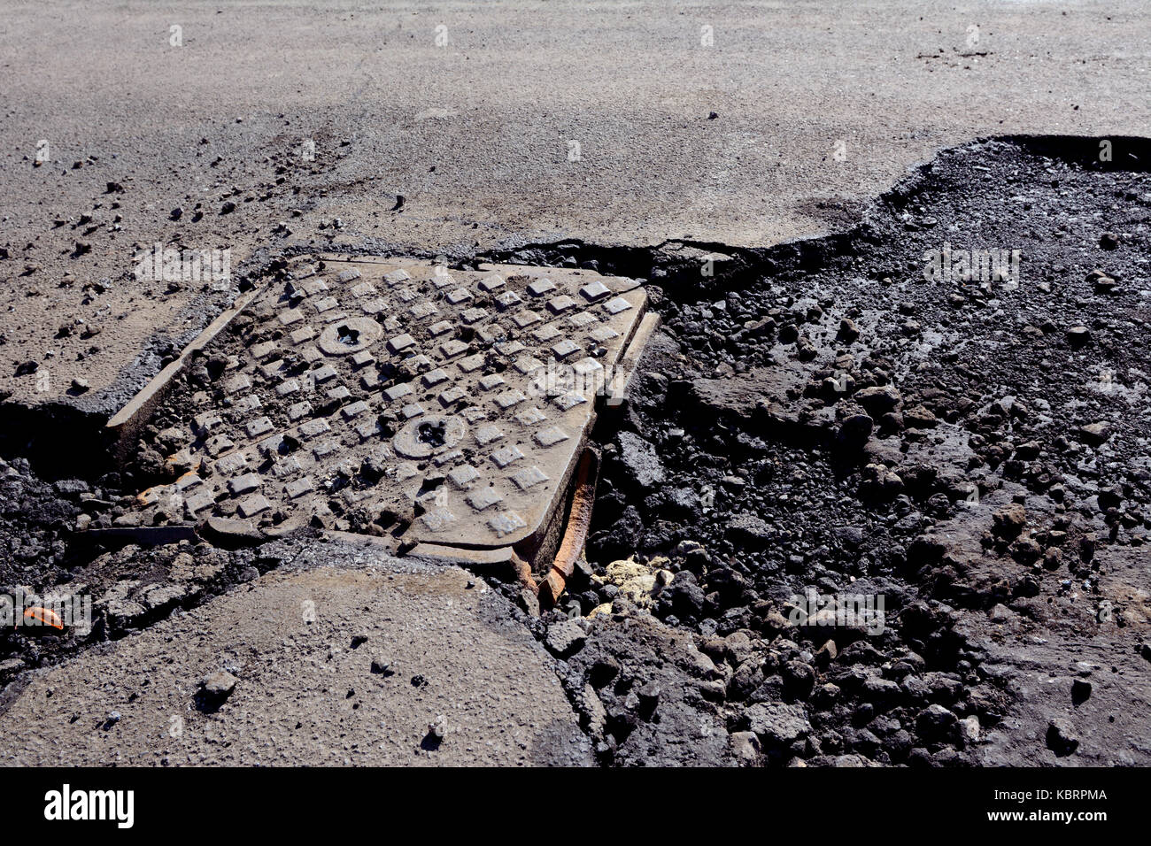 Damaged manhole cover on a road with broken asphalt, undergoing street ...