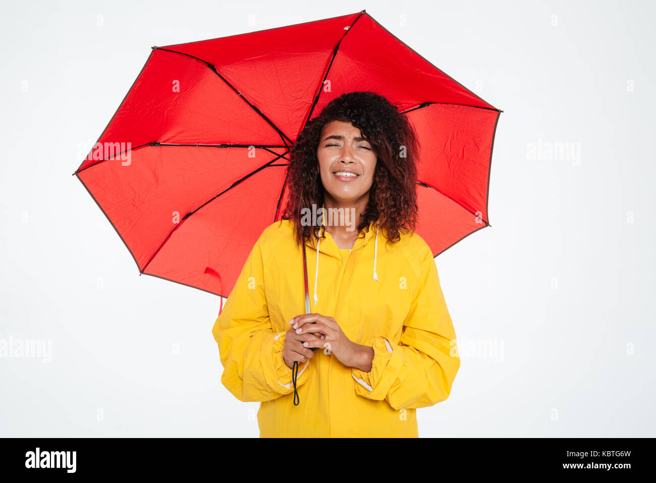Tired african woman in raincoat crying while hiding under umbrella over ...
