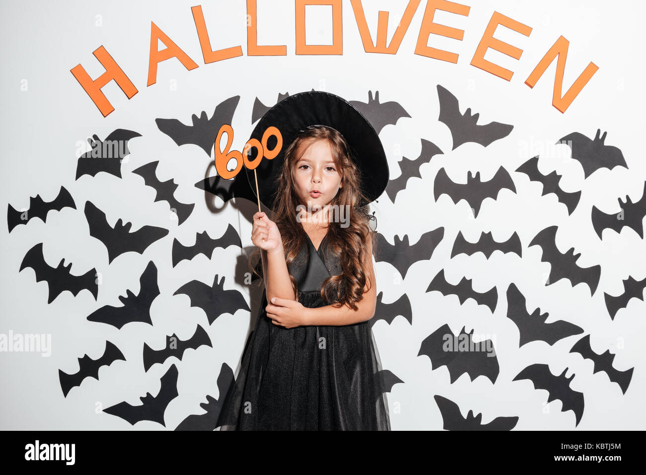 Pretty little girl dressed in halloween costume holding mask and posing ...