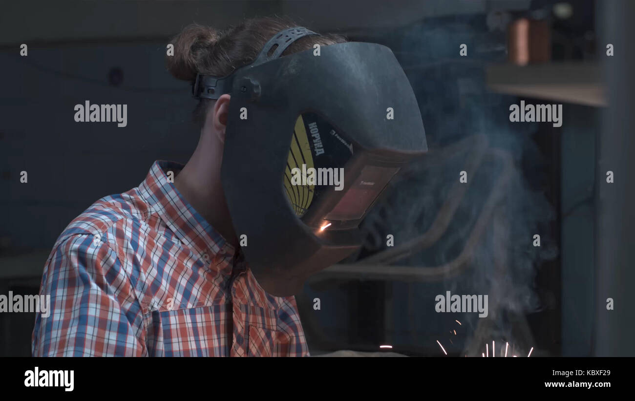 Young man with protective mask welding in a factory. A young brunette ...