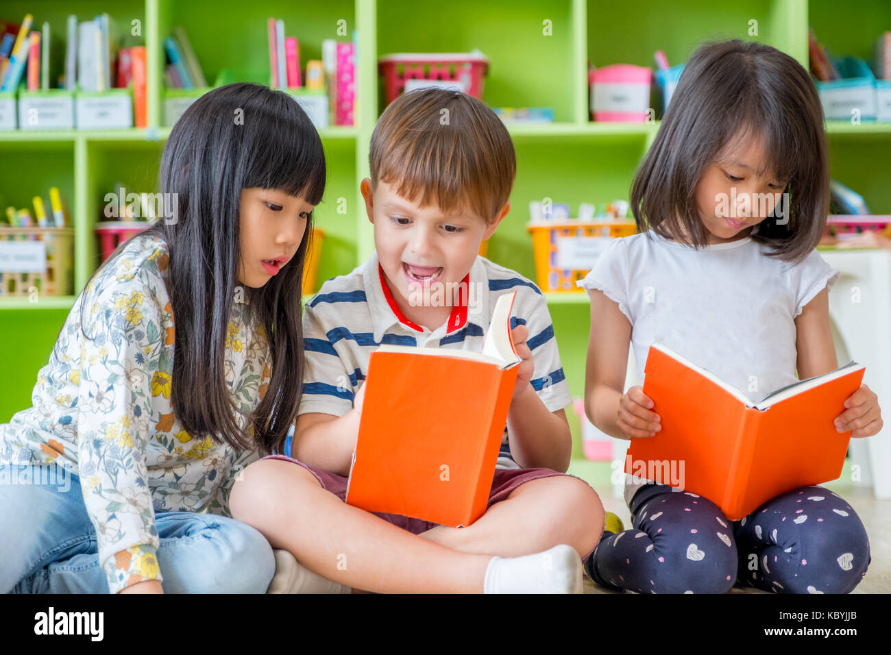 Children sitting on floor and reading tale book in preschool library ...
