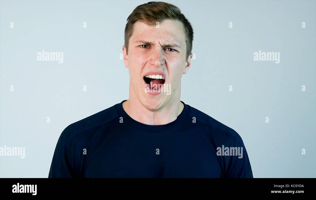 An young man yells at the camera with black t-shirt and grey background ...