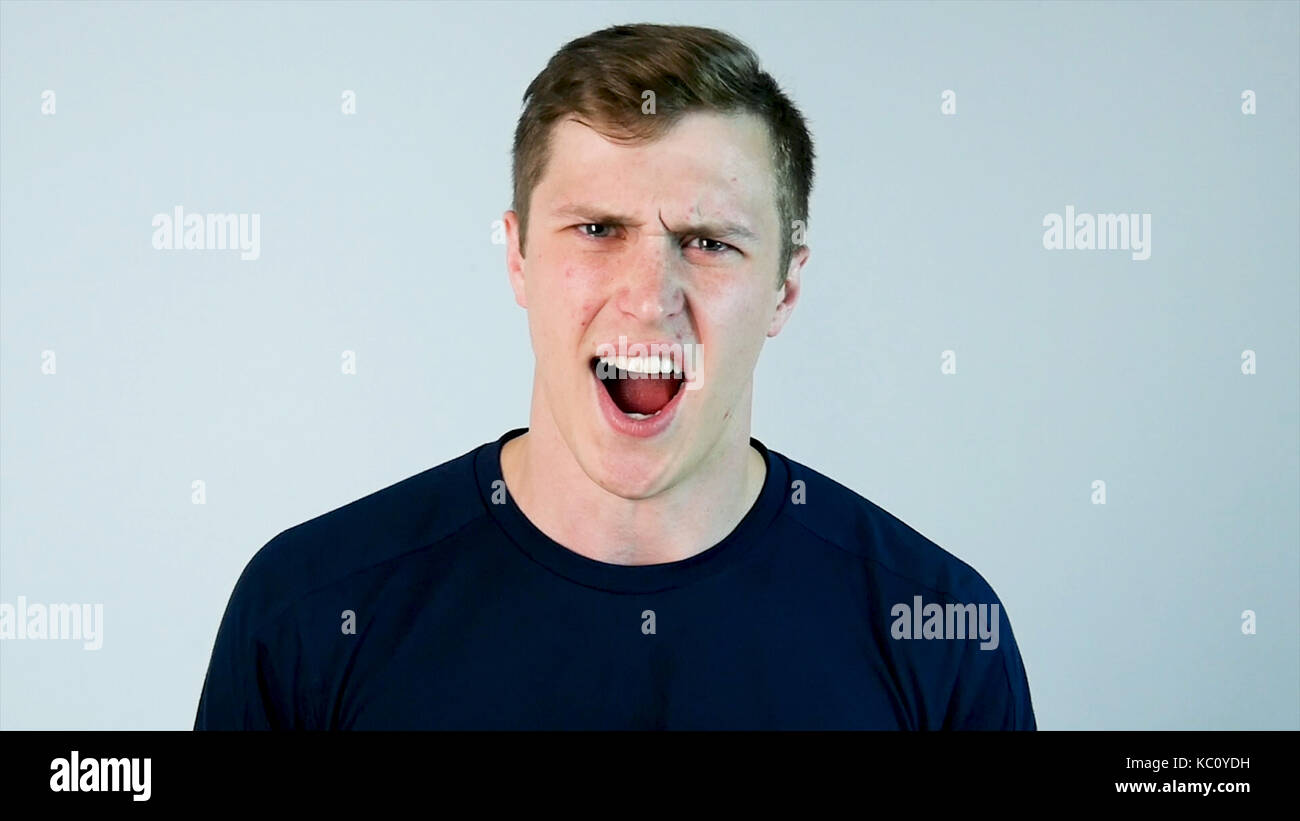 An young man yells at the camera with black t-shirt and grey background ...