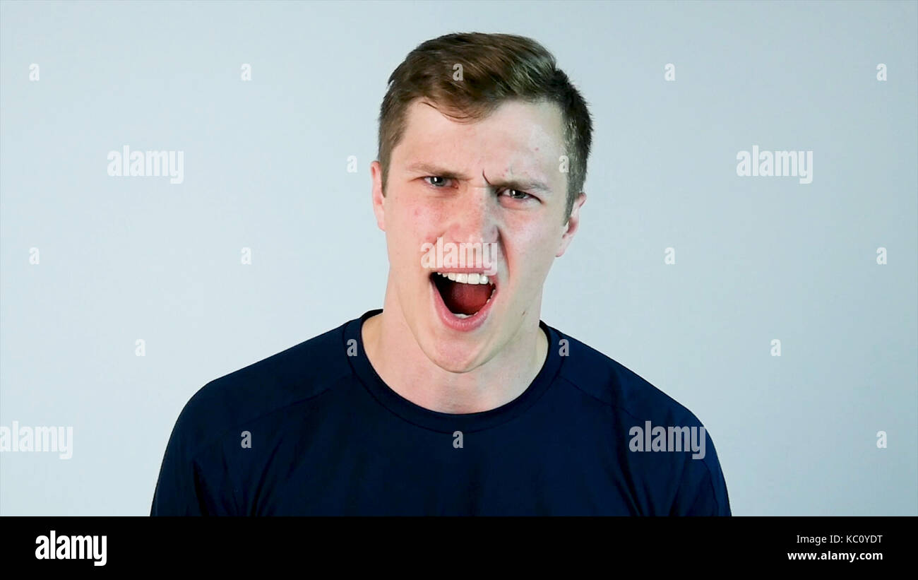 An young man yells at the camera with black t-shirt and grey background ...