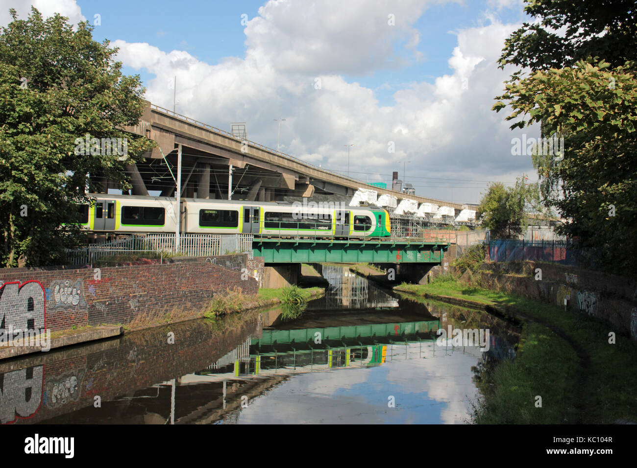 A London Midland train is reflected in the water as it crosses a canal ...
