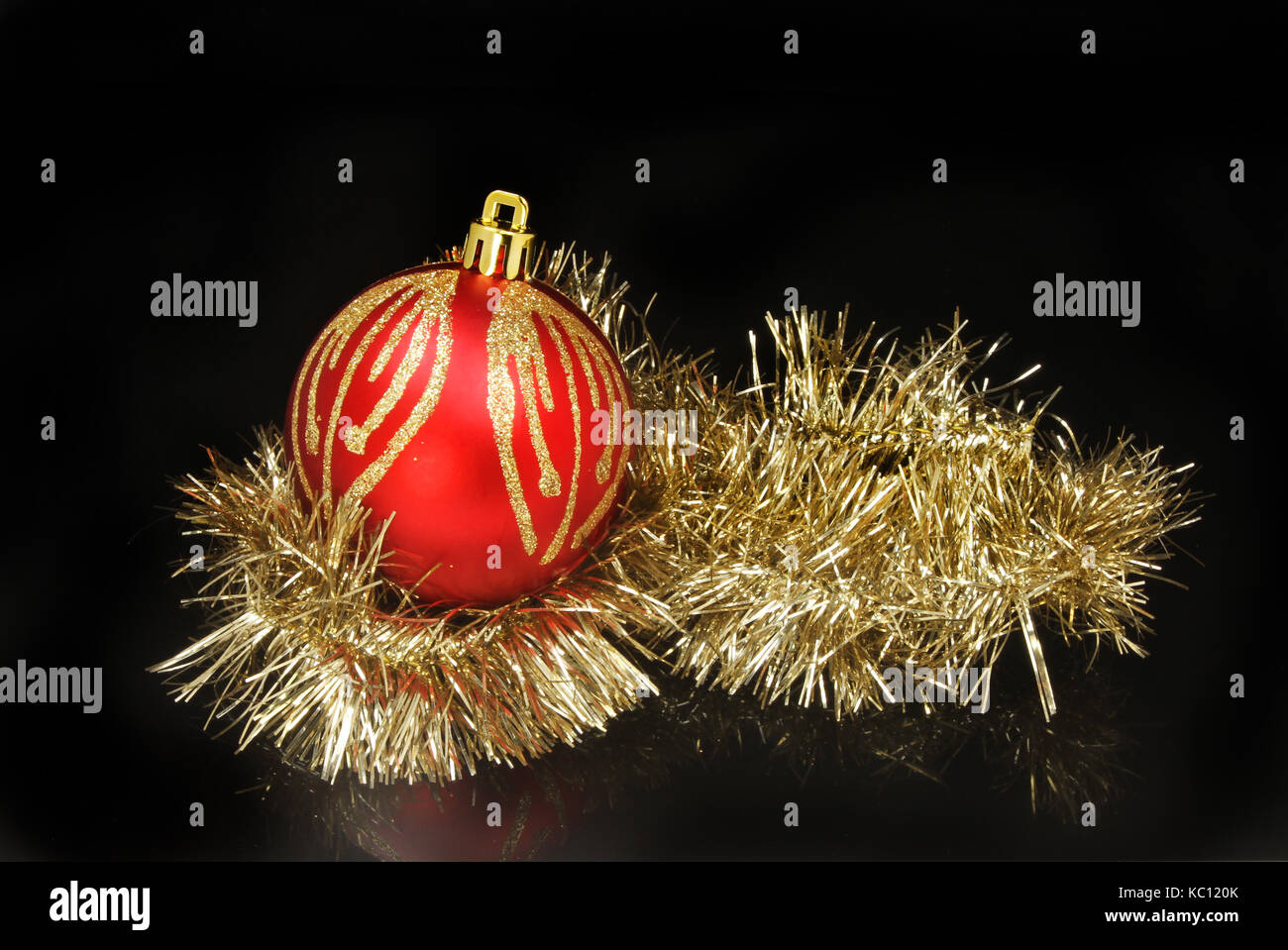 Red and gold glitter Christmas bauble and tinsel against a black ...