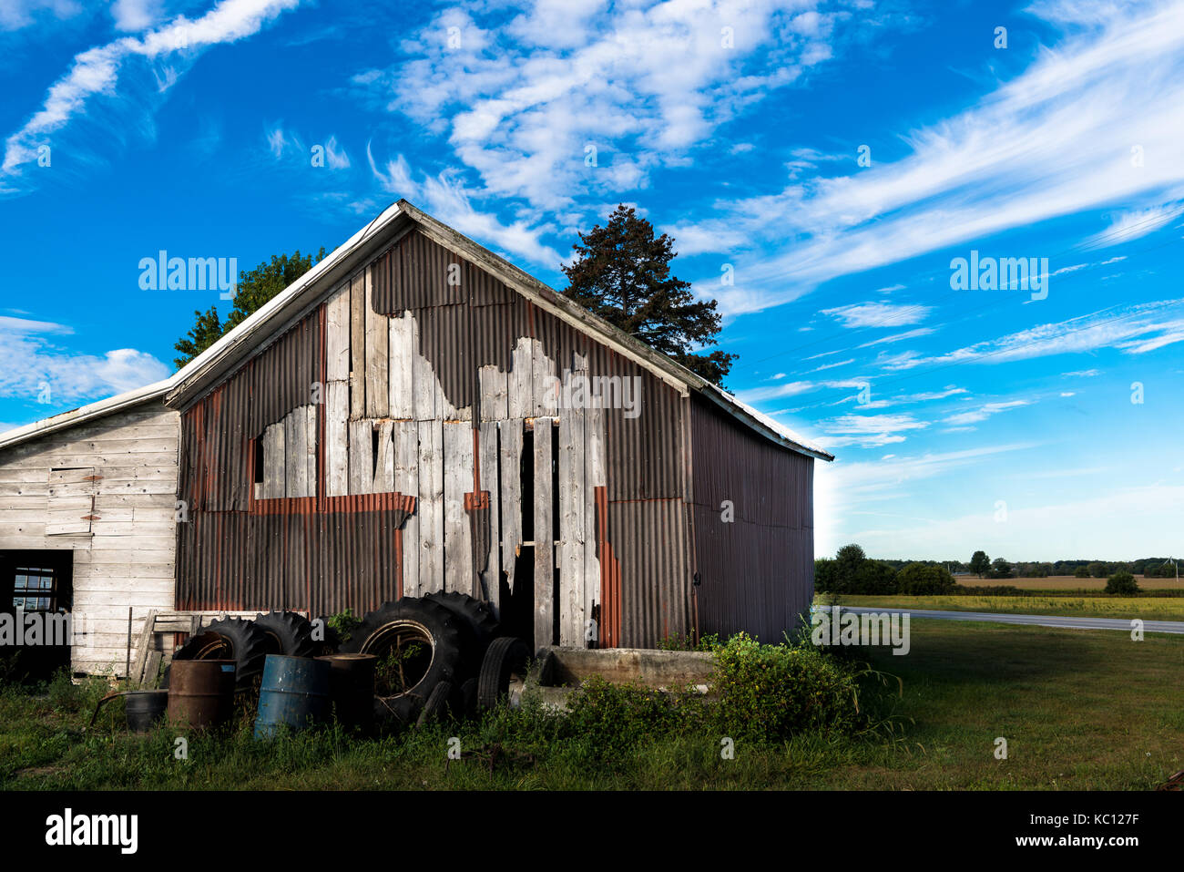 Vintage barn with barrels and tires in front. the sky is blue with ...