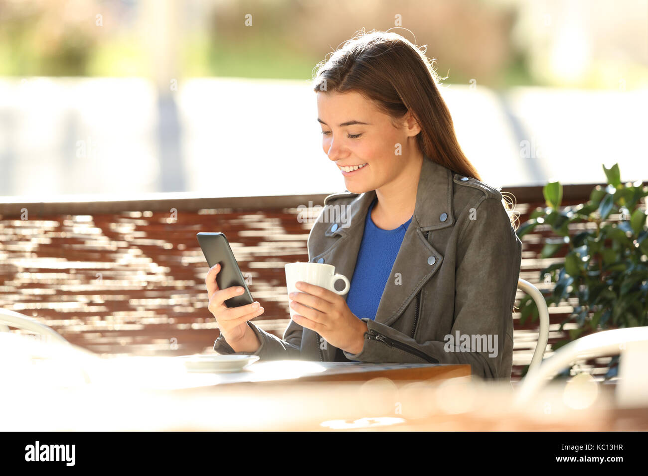 Single fashion teen using a smart phone sitting in a coffee shop ...