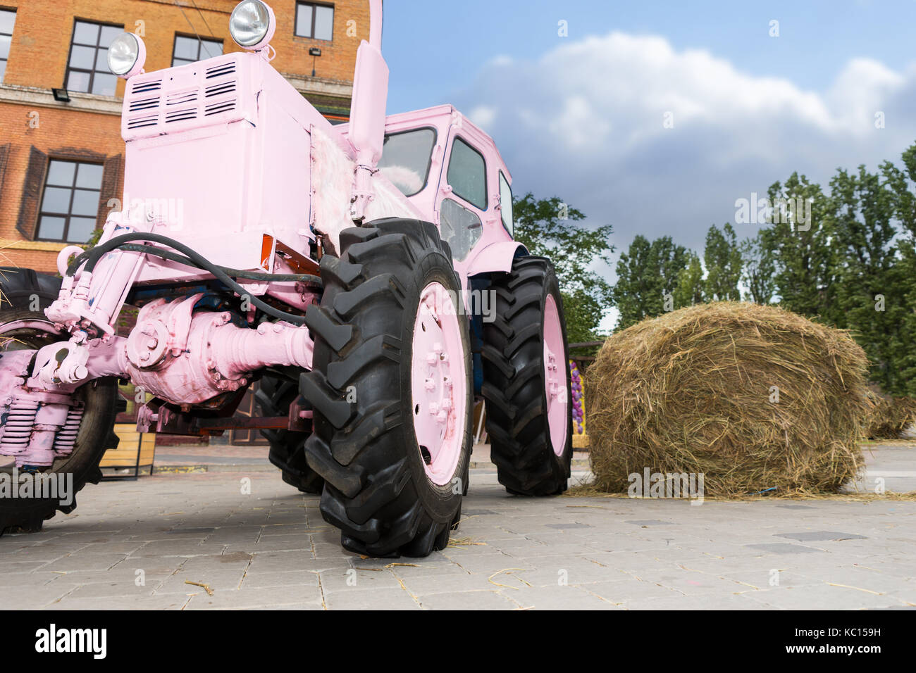 Fancy pink tractor next to a haystack, old brick building in the ...
