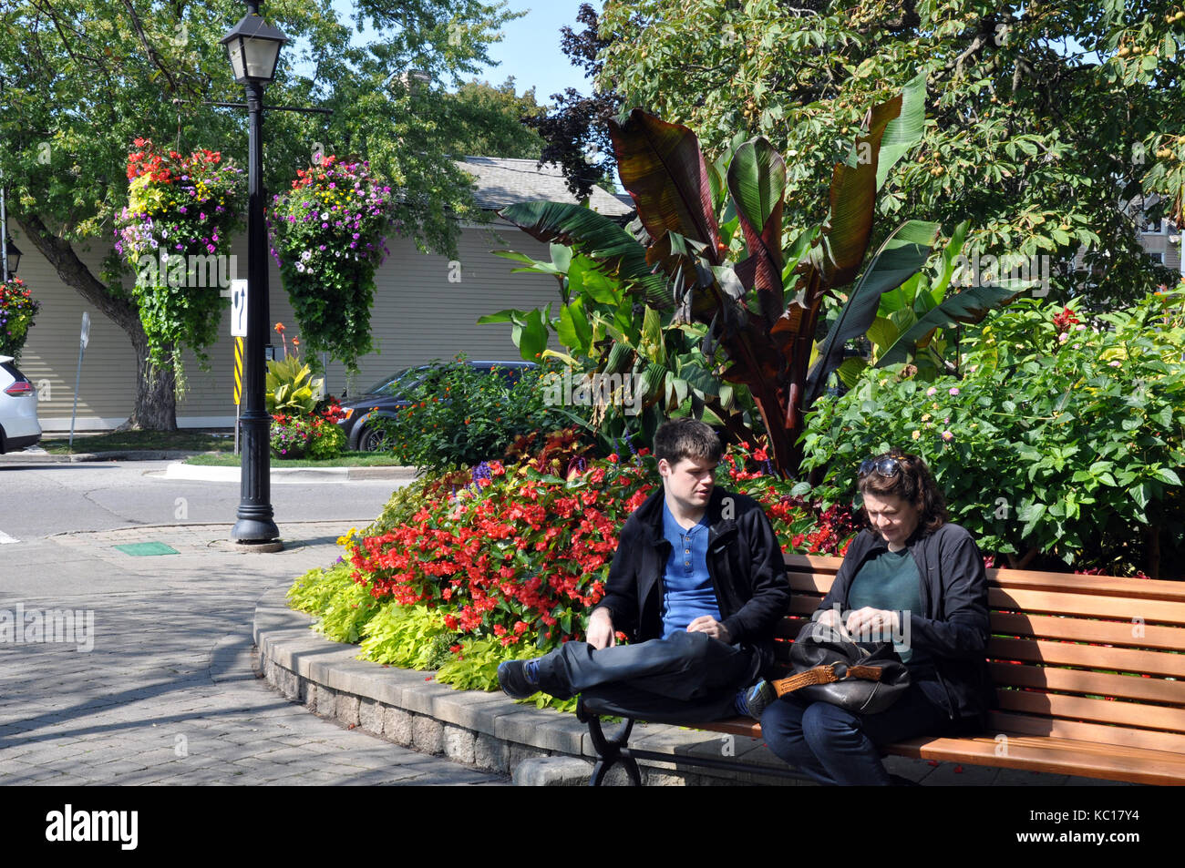 Two People Seated on a Bench in a City Park with Gardens in background ...