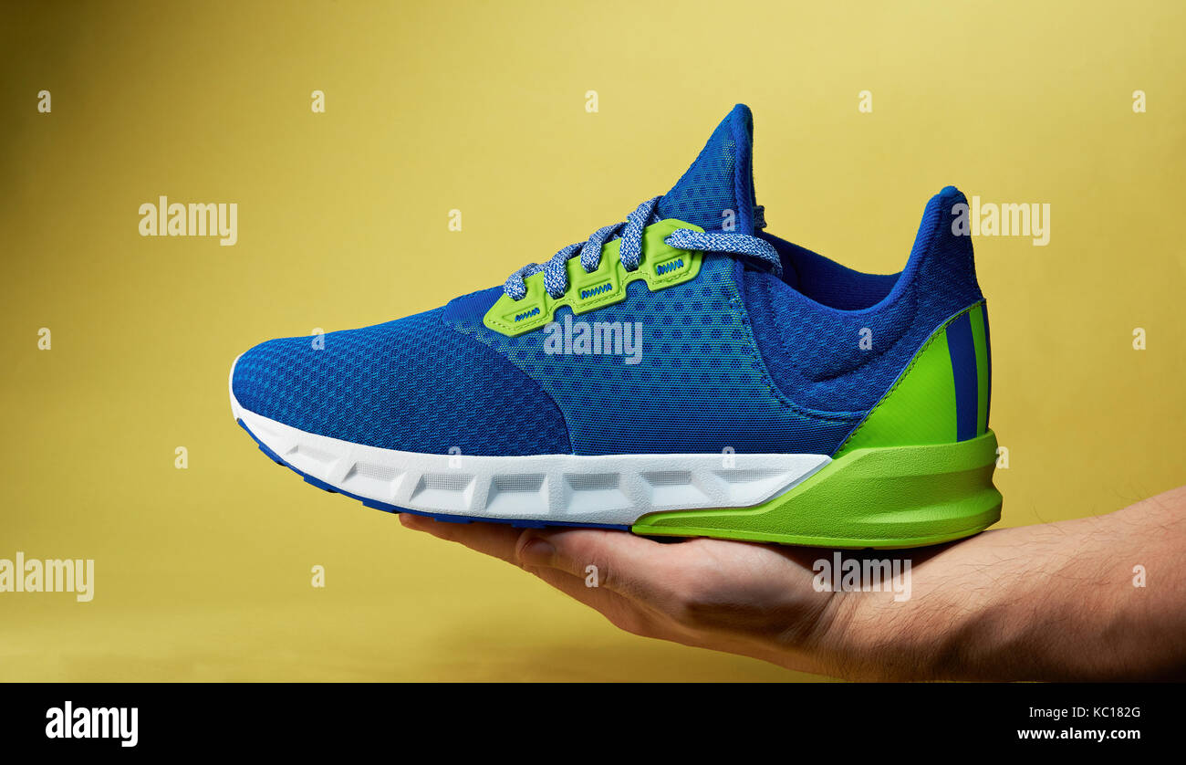 Sport shoe on hand isolated on yellow background. Hand keep one running ...
