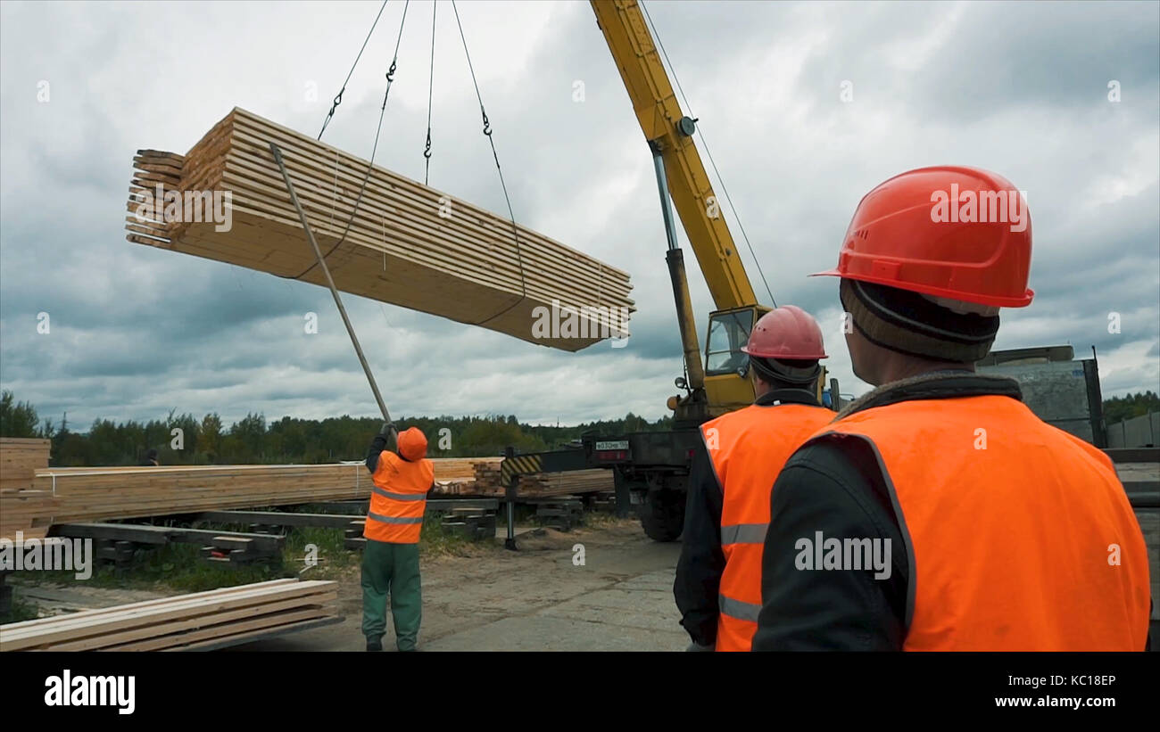 Workers transporting a wooden bars using crane. Worker in a ...