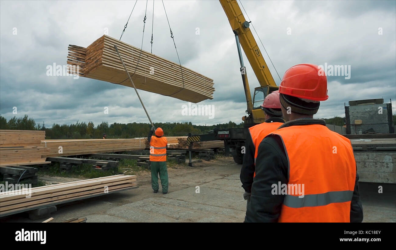 Workers transporting a wooden bars using crane. Worker in a ...