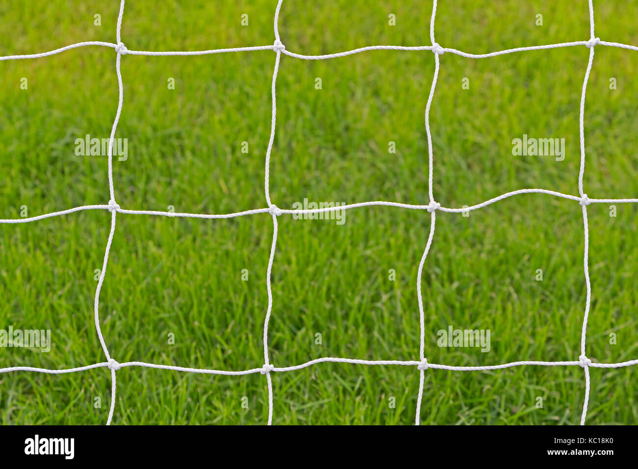 Close up of a white goal net with grass out of focus in the background ...