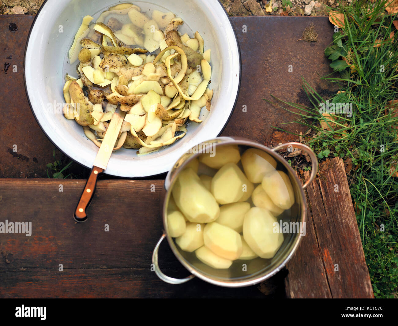 Peeled potato in a casserole and potato skin in a food bowl. Wooden ...
