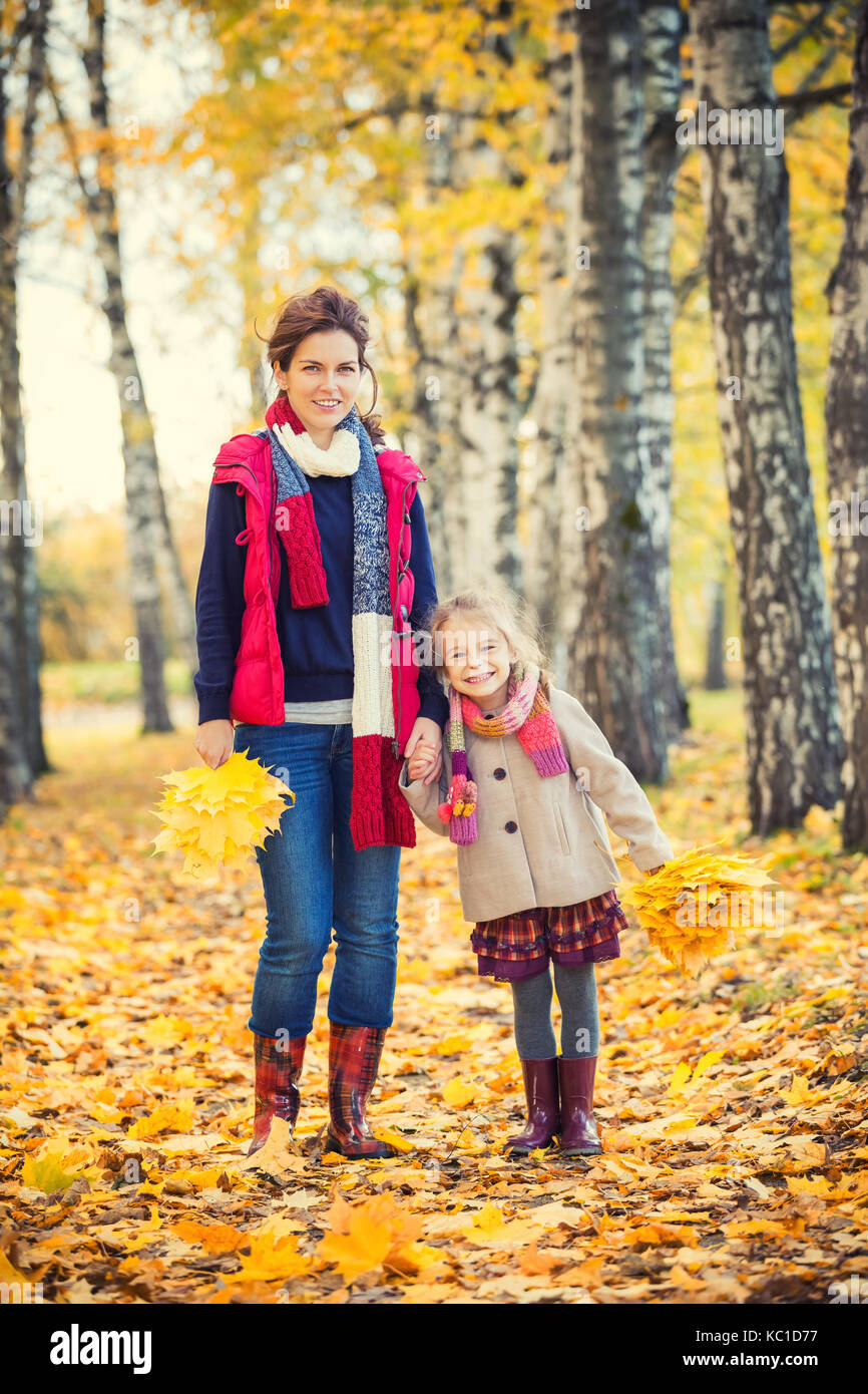 Smiling little girl and her mother enjoy walk in autumn park and play ...