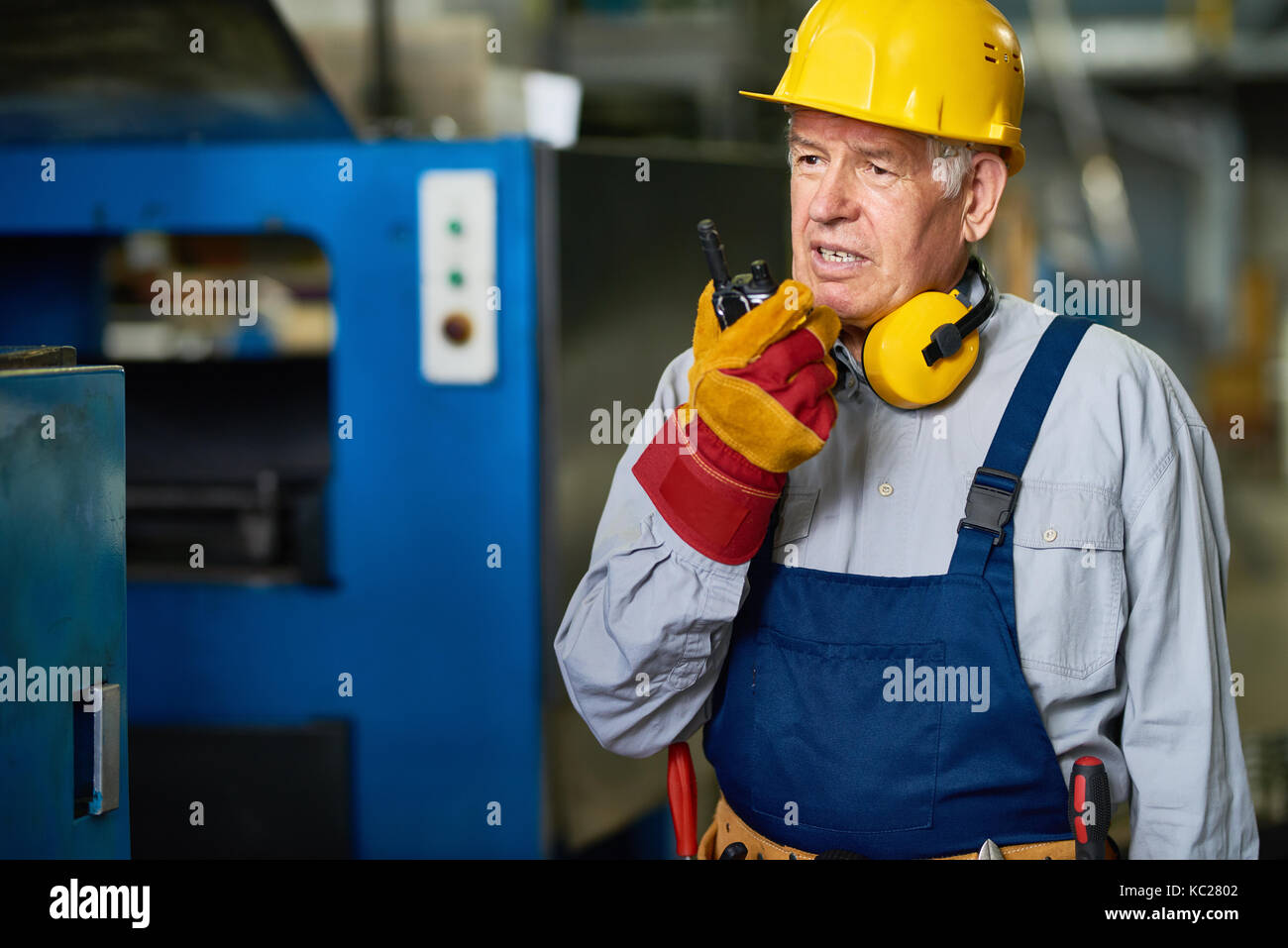 Portrait of senior factory worker using portable radio set talking to ...