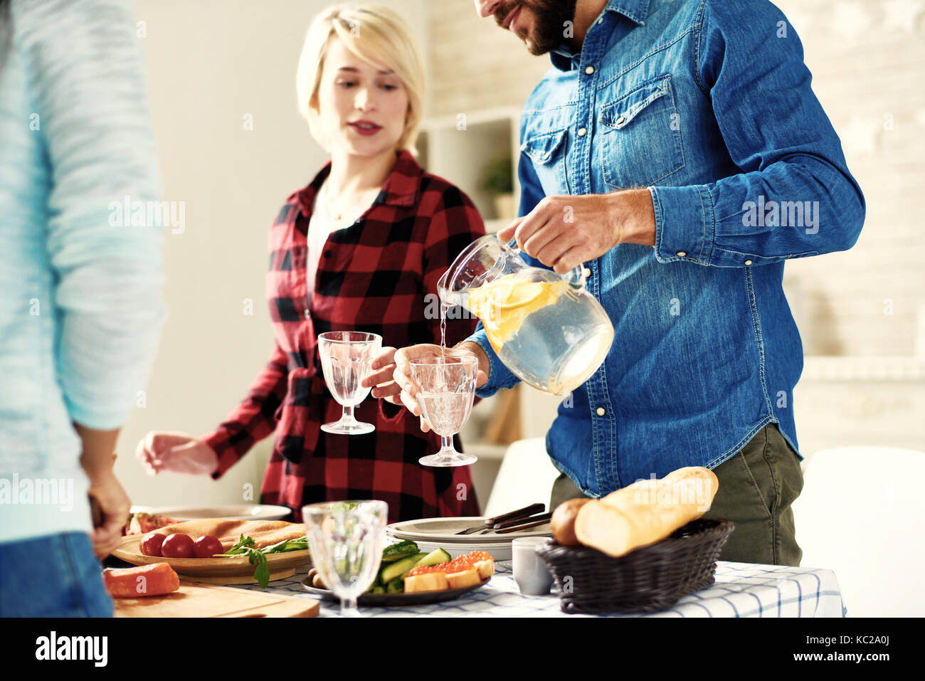 Young man pouring refreshing lemonade to glasses standing at big table ...