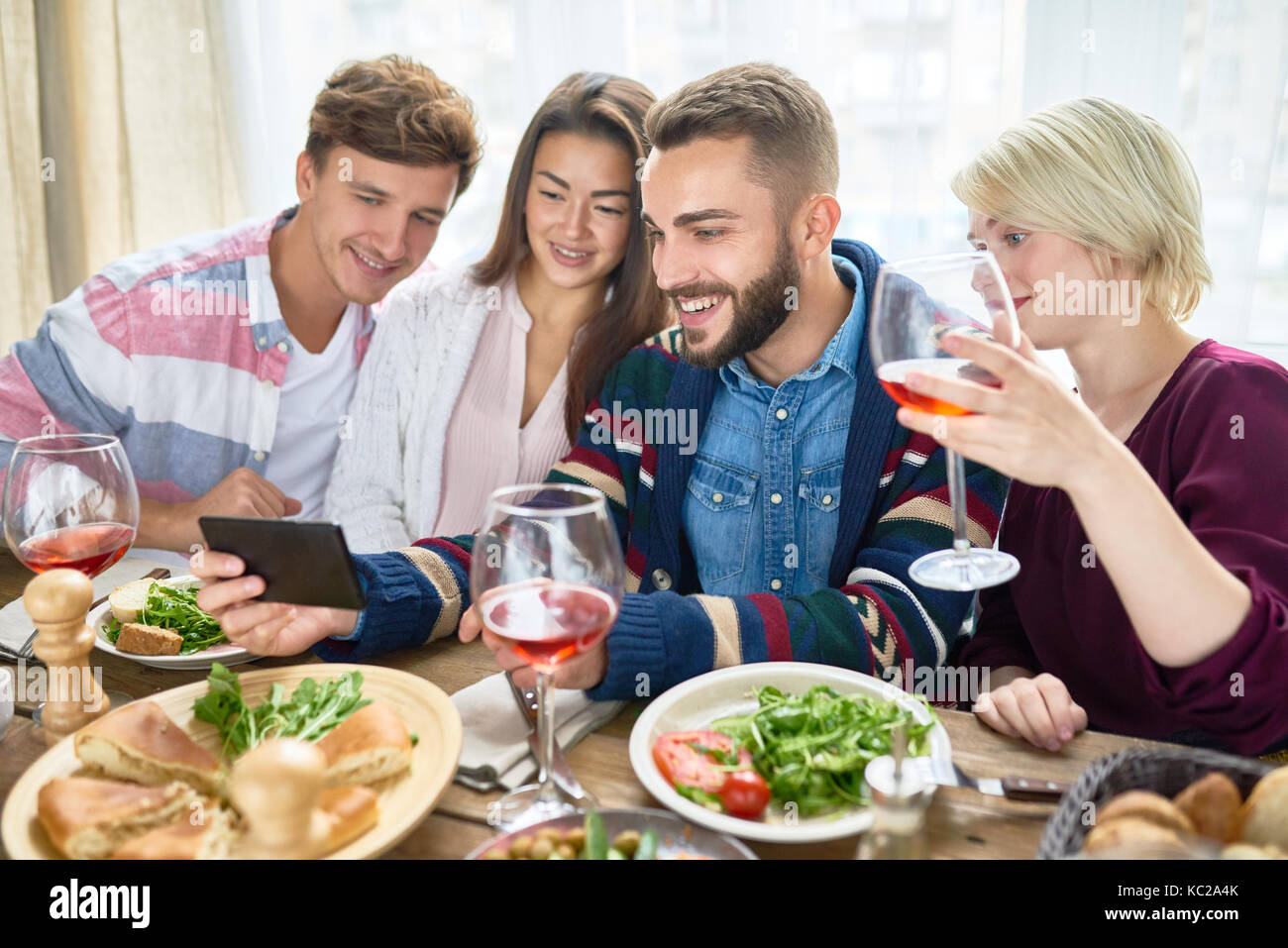 Portrait of four people smiling happily watching videos from smartphone ...