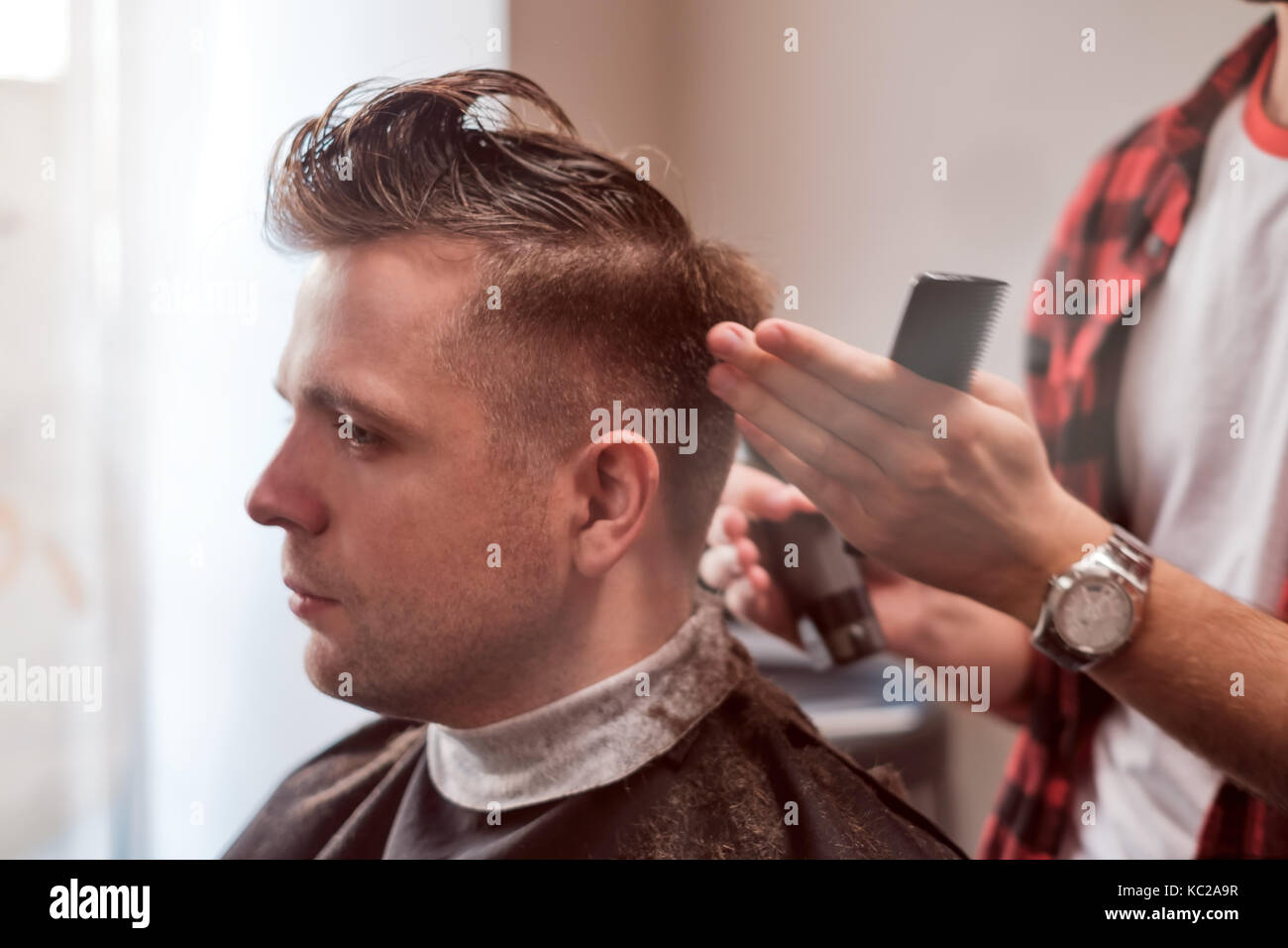 Caucasian young man in Barbershop. Barber is cuttinhg his hair in ...