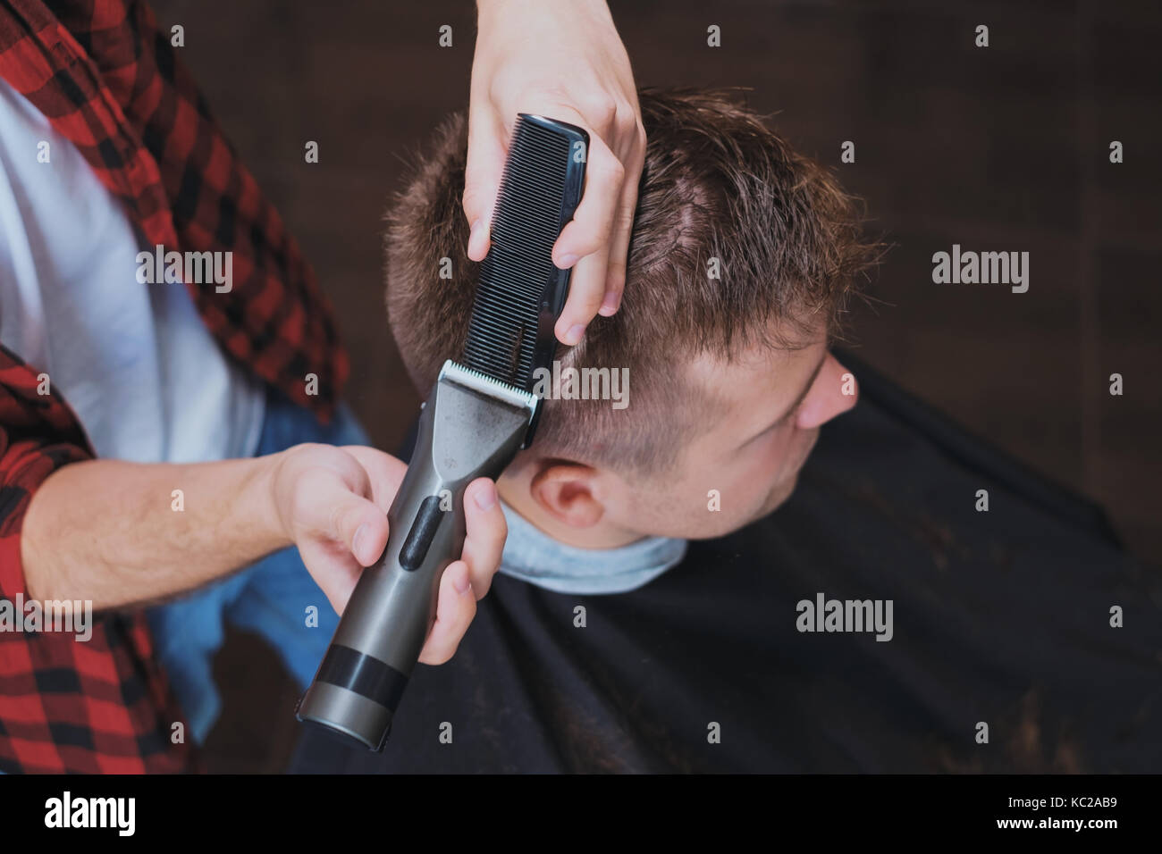 Caucasian young man in Barbershop. Barber is cuttinhg his hair in ...