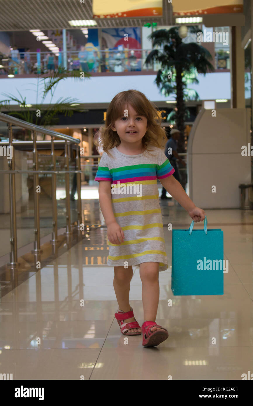 cute little girl is walking along a supermarket with a color package ...