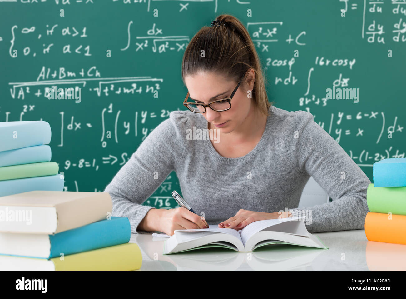 Young Woman Writing With Pen In Book At Desk Stock Photo - Alamy