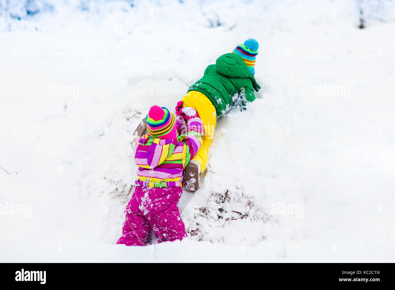 Kids playing in snow. Children climb up a snow hill. Sister helping ...