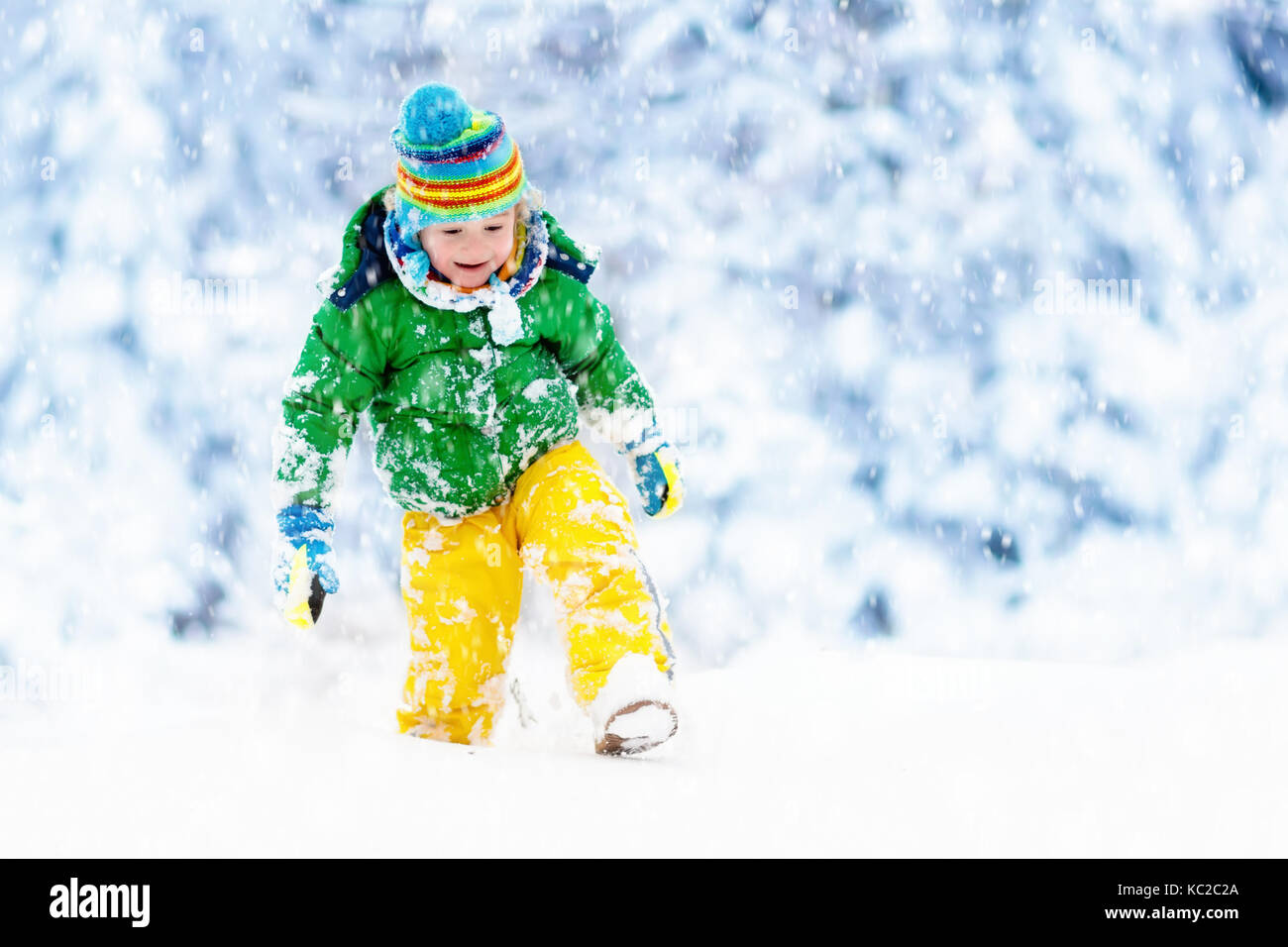 Child playing with snow in winter. Little boy in colorful jacket and ...