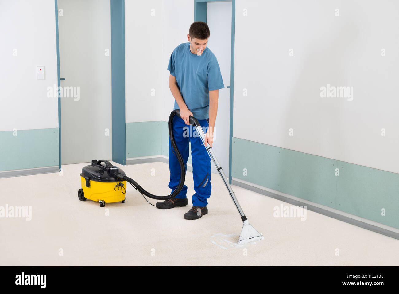 Young Male Cleaner In Uniform Vacuuming Floor Stock Photo - Alamy