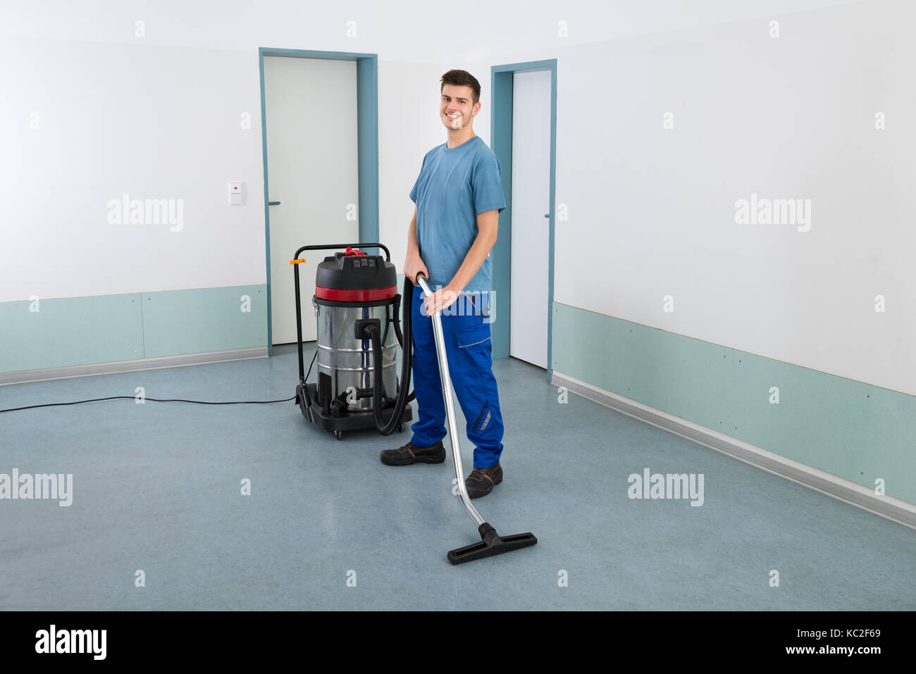 Young Happy Male Worker Cleaning Floor With Vacuum Cleaner Stock Photo ...