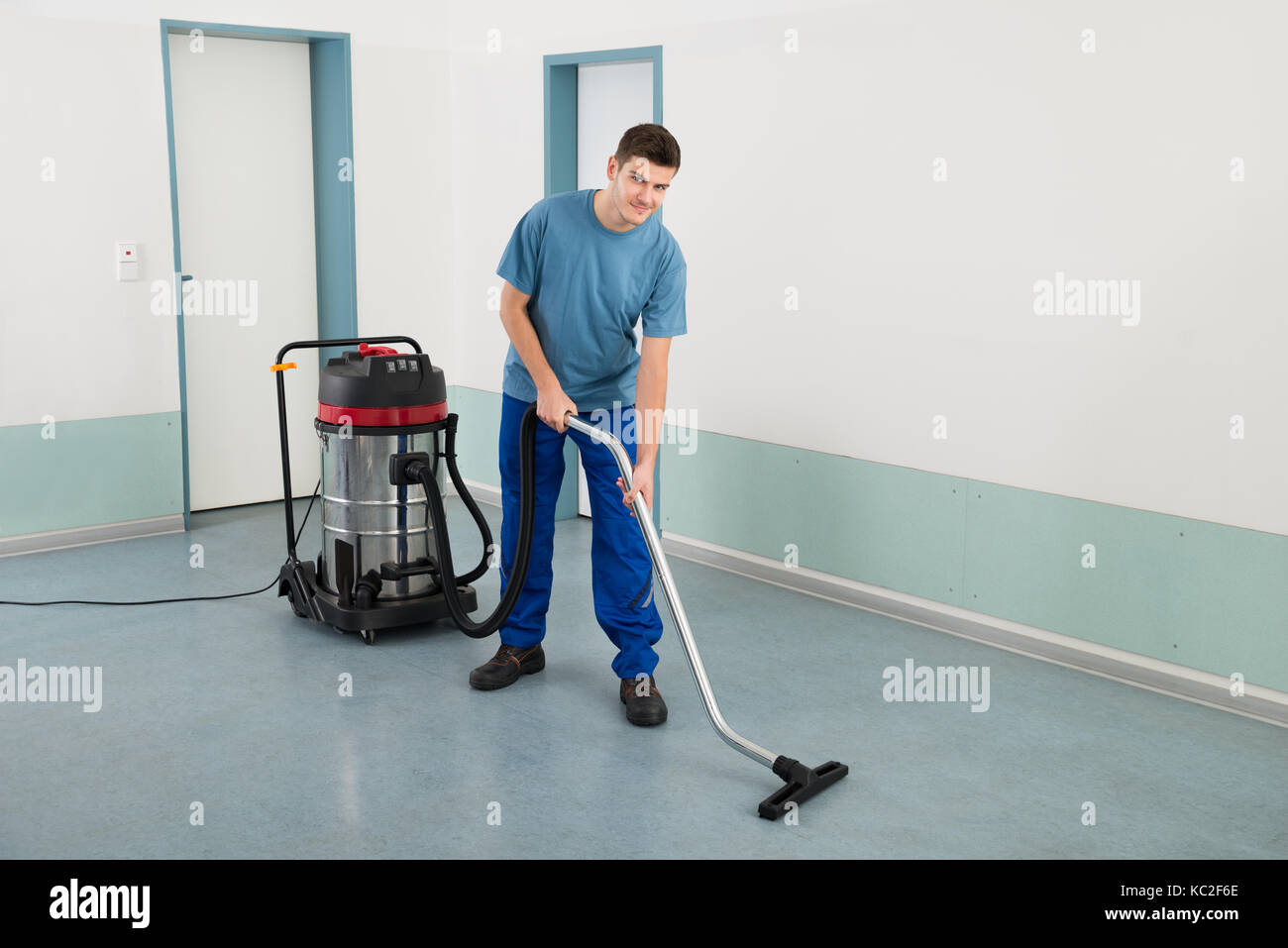 Young Happy Male Worker Cleaning Floor With Vacuum Cleaner Stock Photo ...