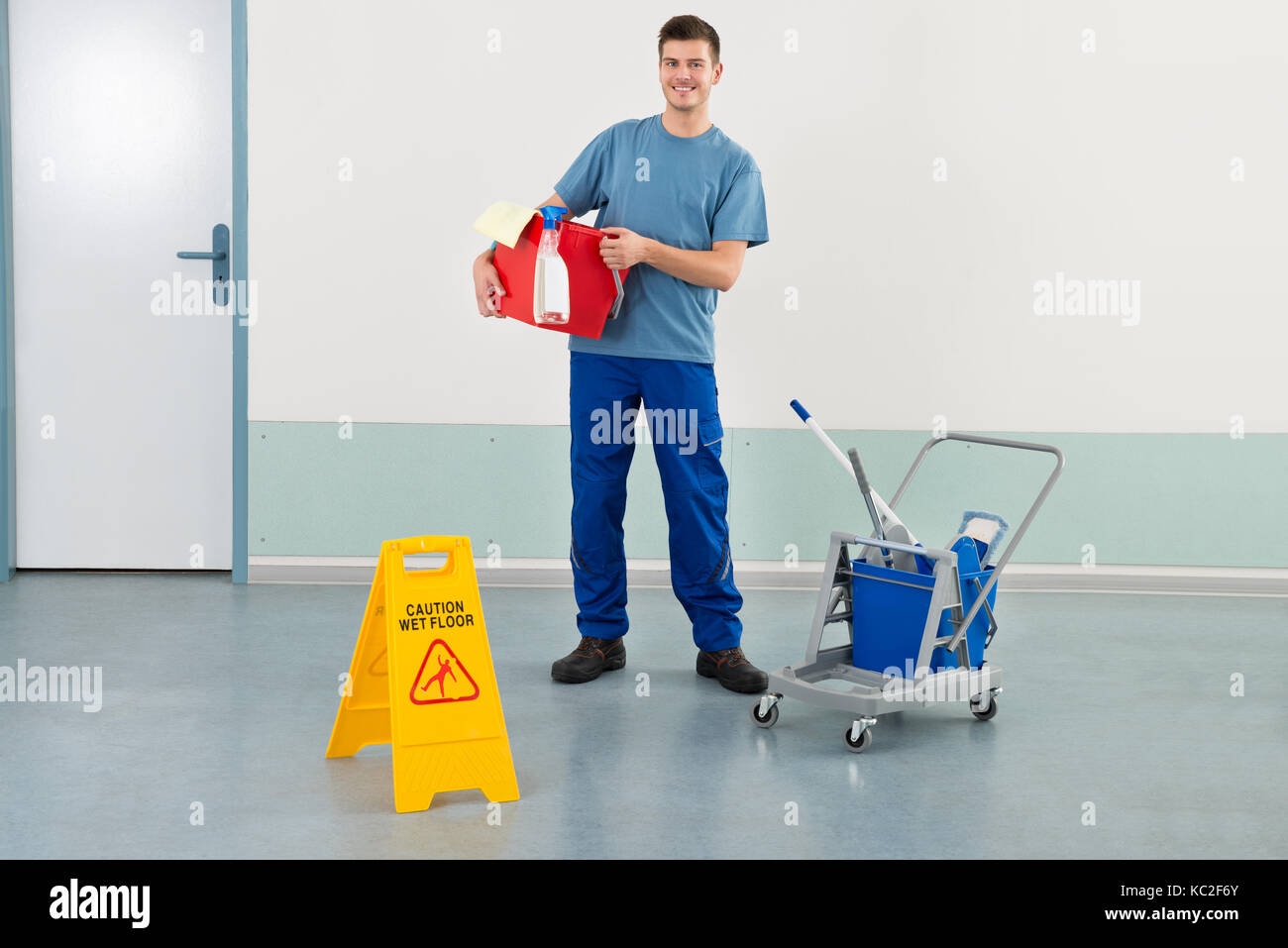 Happy Male Worker With Cleaning Equipments And Wet Floor Caution Sign ...