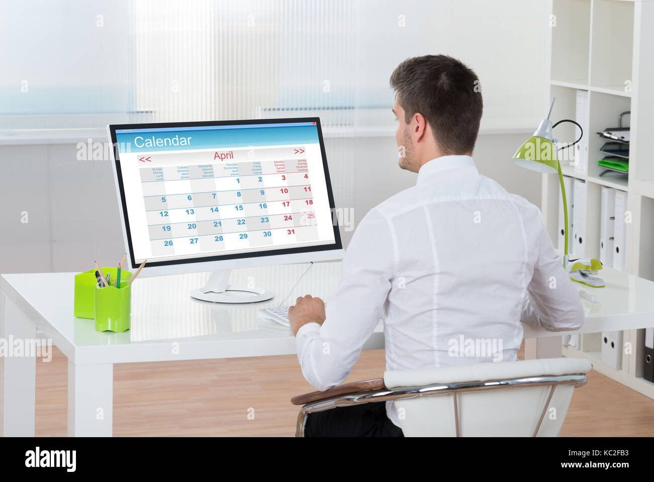 Young Businessman Looking At Calendar On Computer At Desk Stock Photo ...