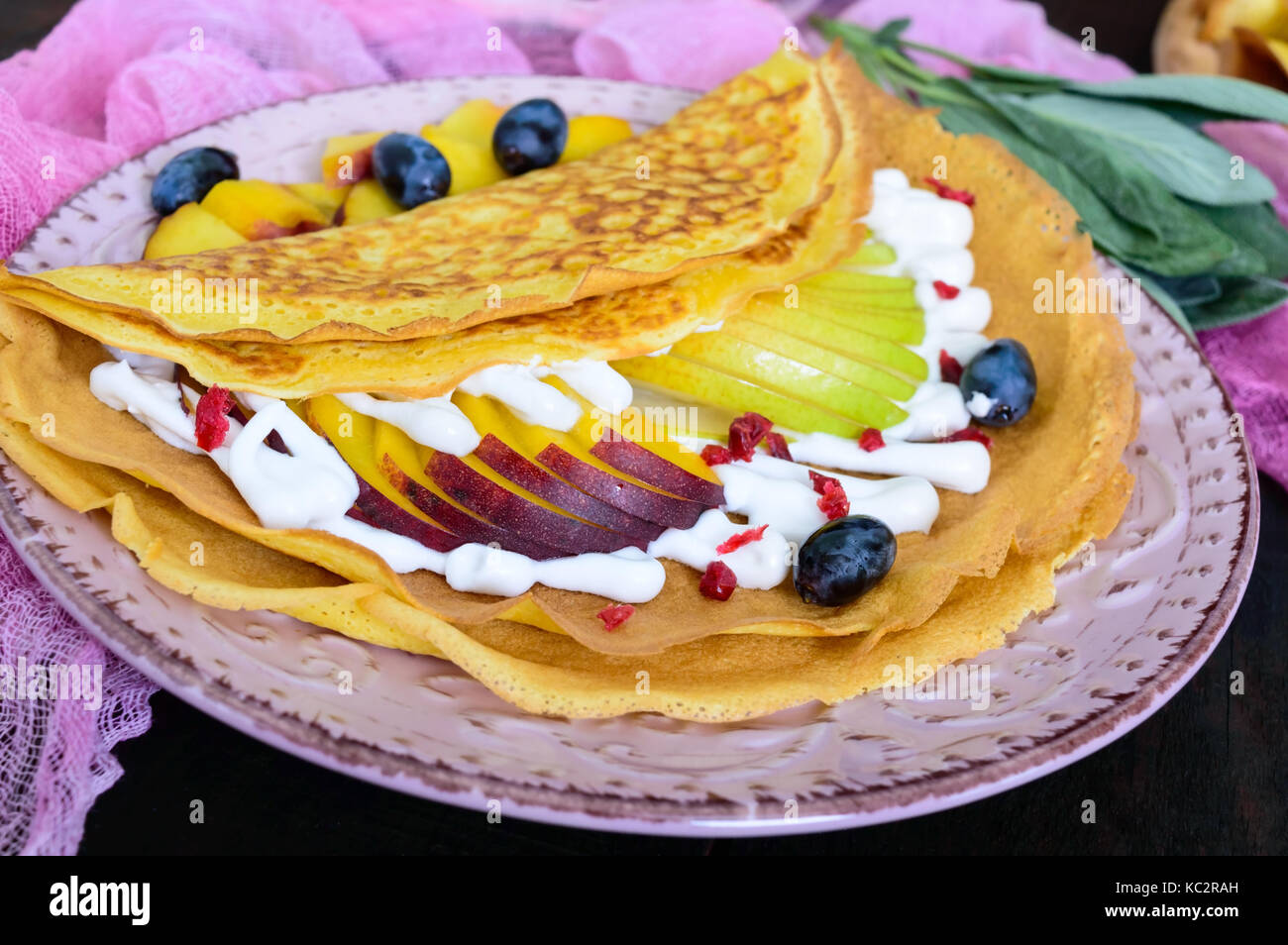 Golden crepes with pieces of peach, pear, cream and grapes on a ceramic ...