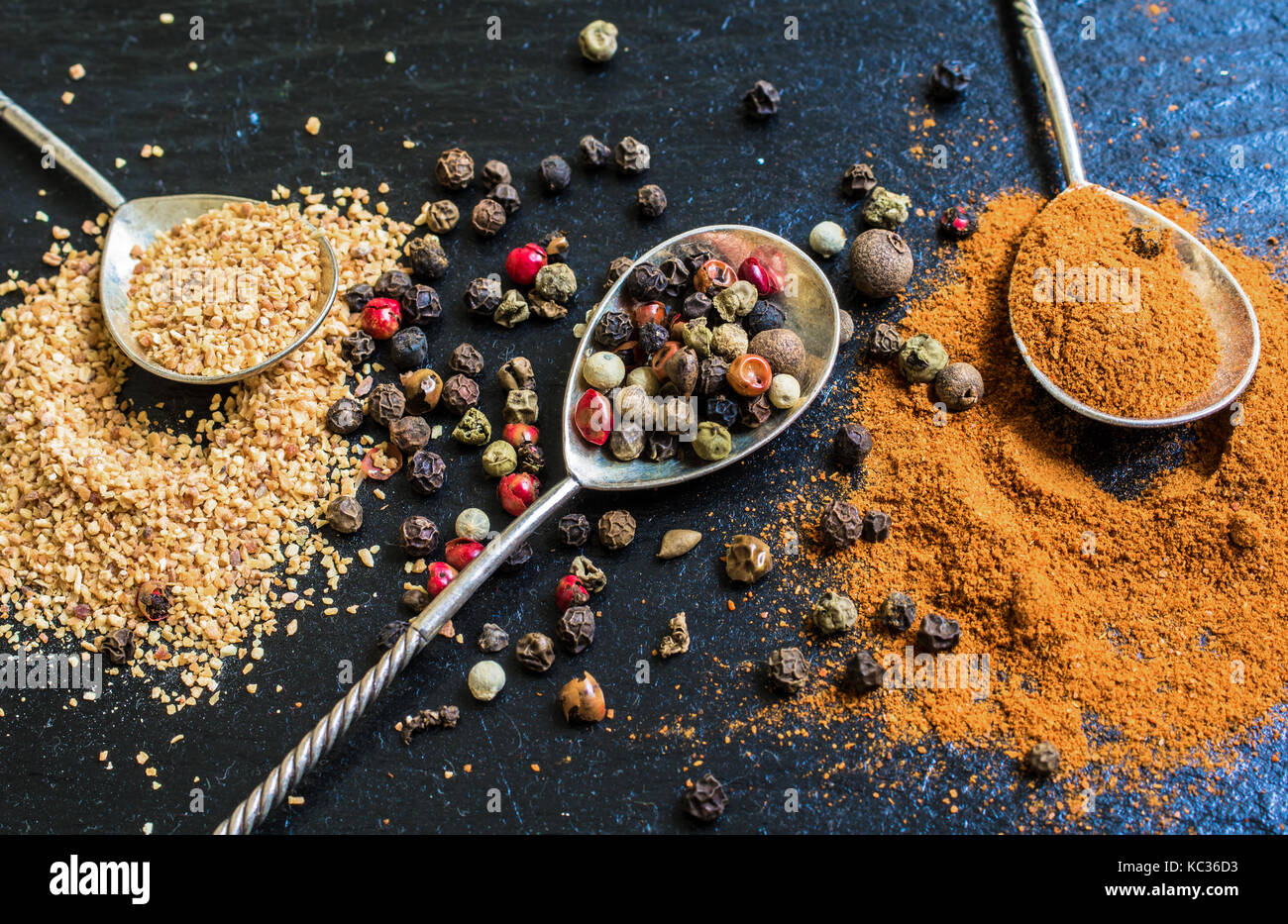 Different types of pepper spice in vintage spoons on black stone ...