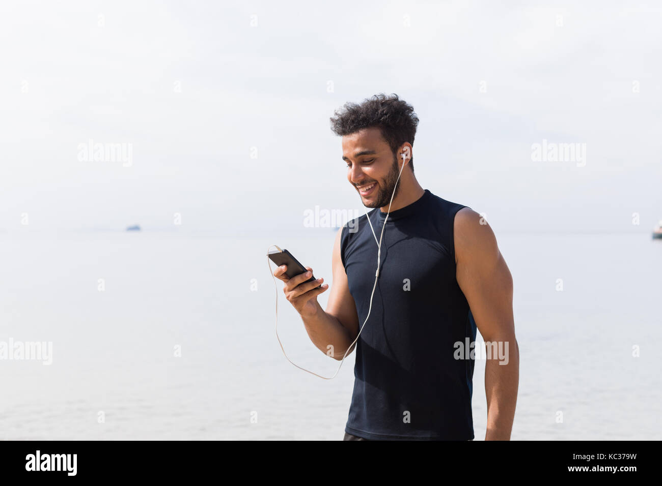 Hispanic Male Runner Using Cell Smart Phone On Beach While Jogging On ...