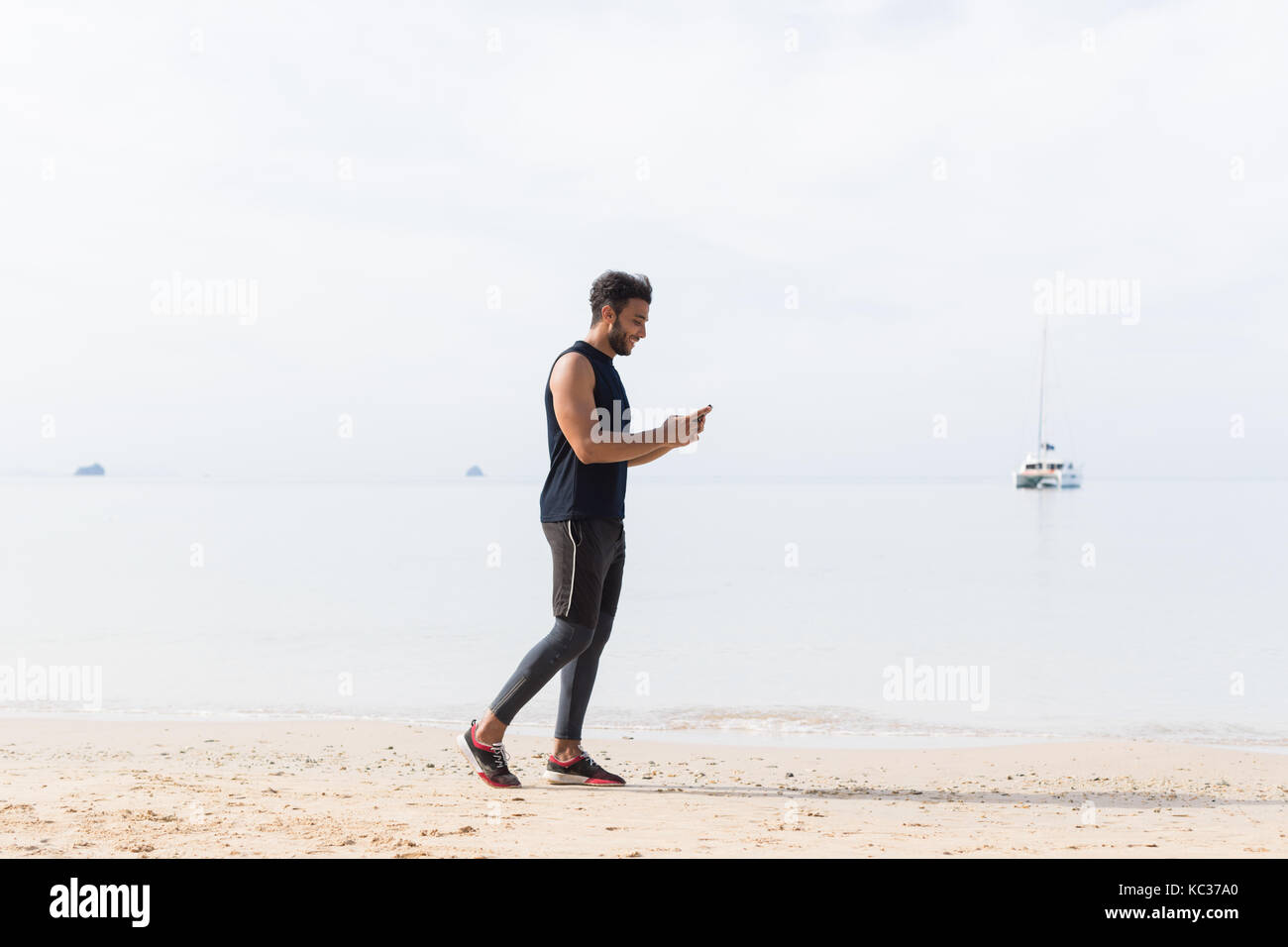 Full Length Shot Of Male Runner Using Cell Smart Phone On Beach While ...