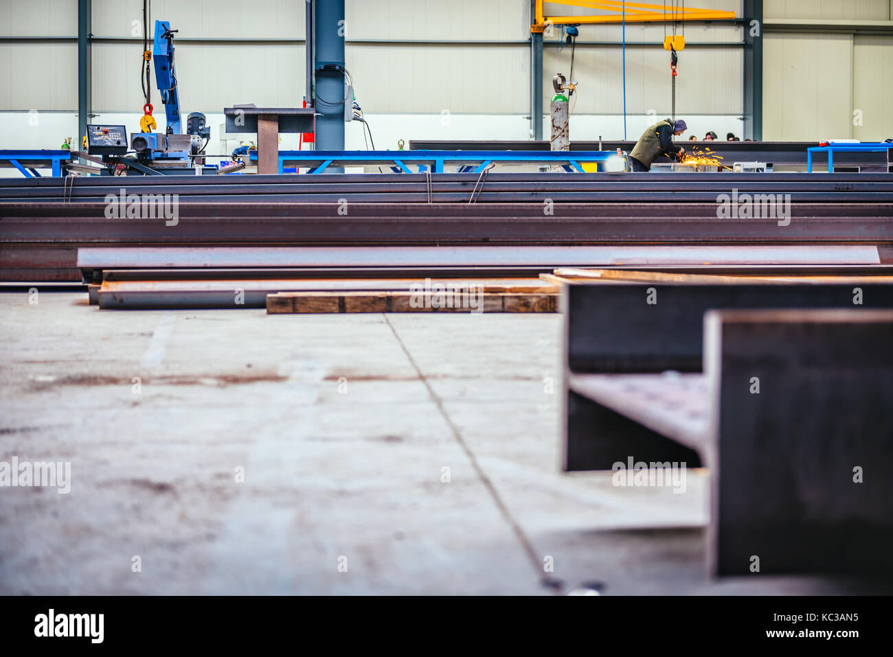Worker grinding in big industrial hall with metal profiles and machines ...