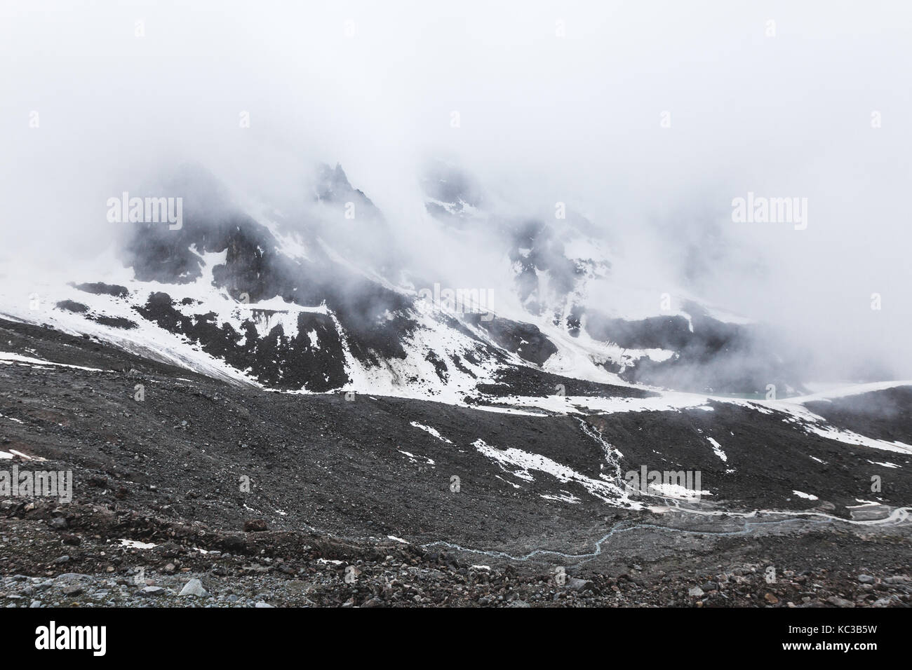 Mountain landscape with rocks and creeping fog. High snow peaks in the ...