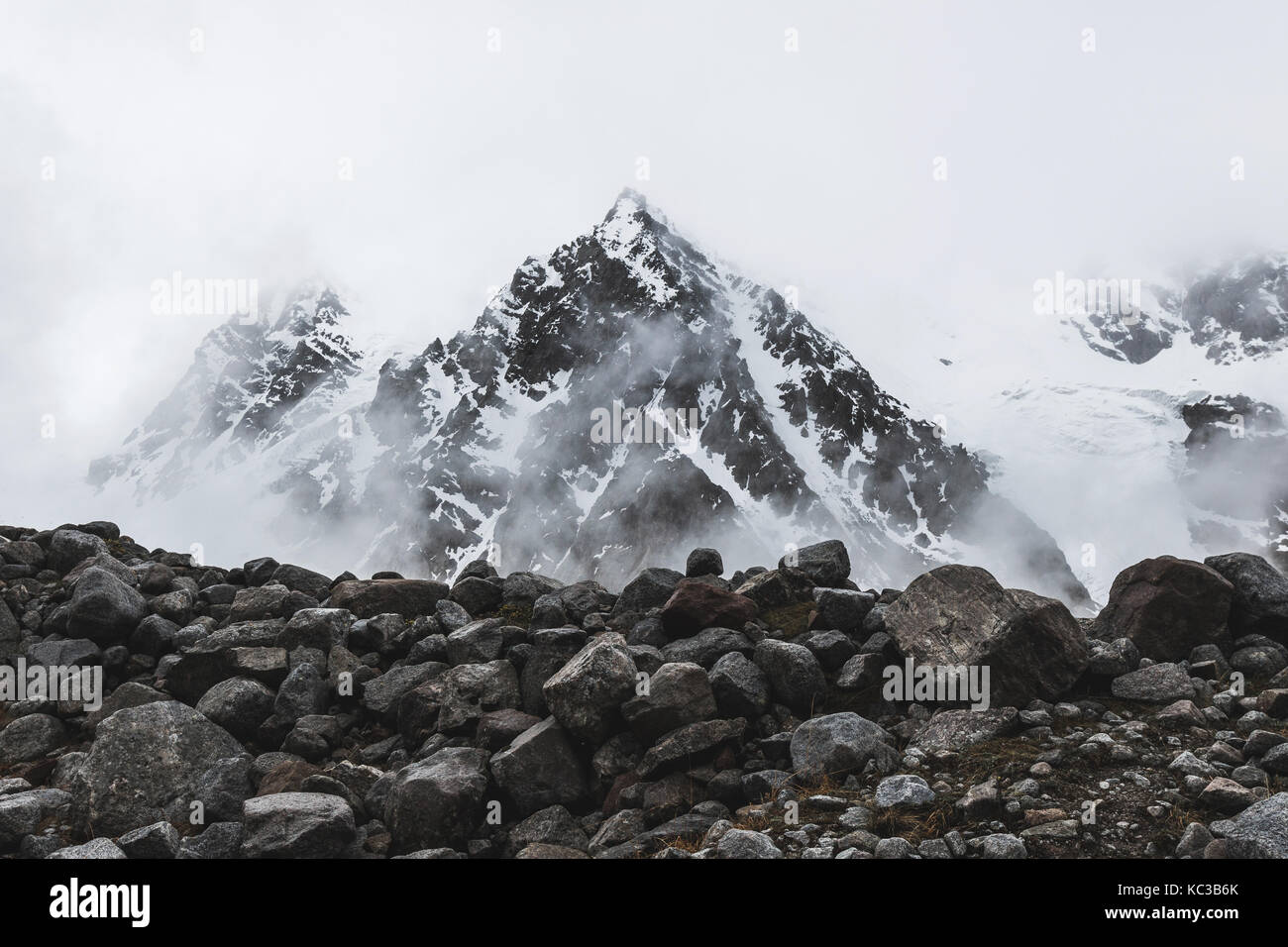 Mountain landscape with rocks and creeping fog. High snow peaks in the ...