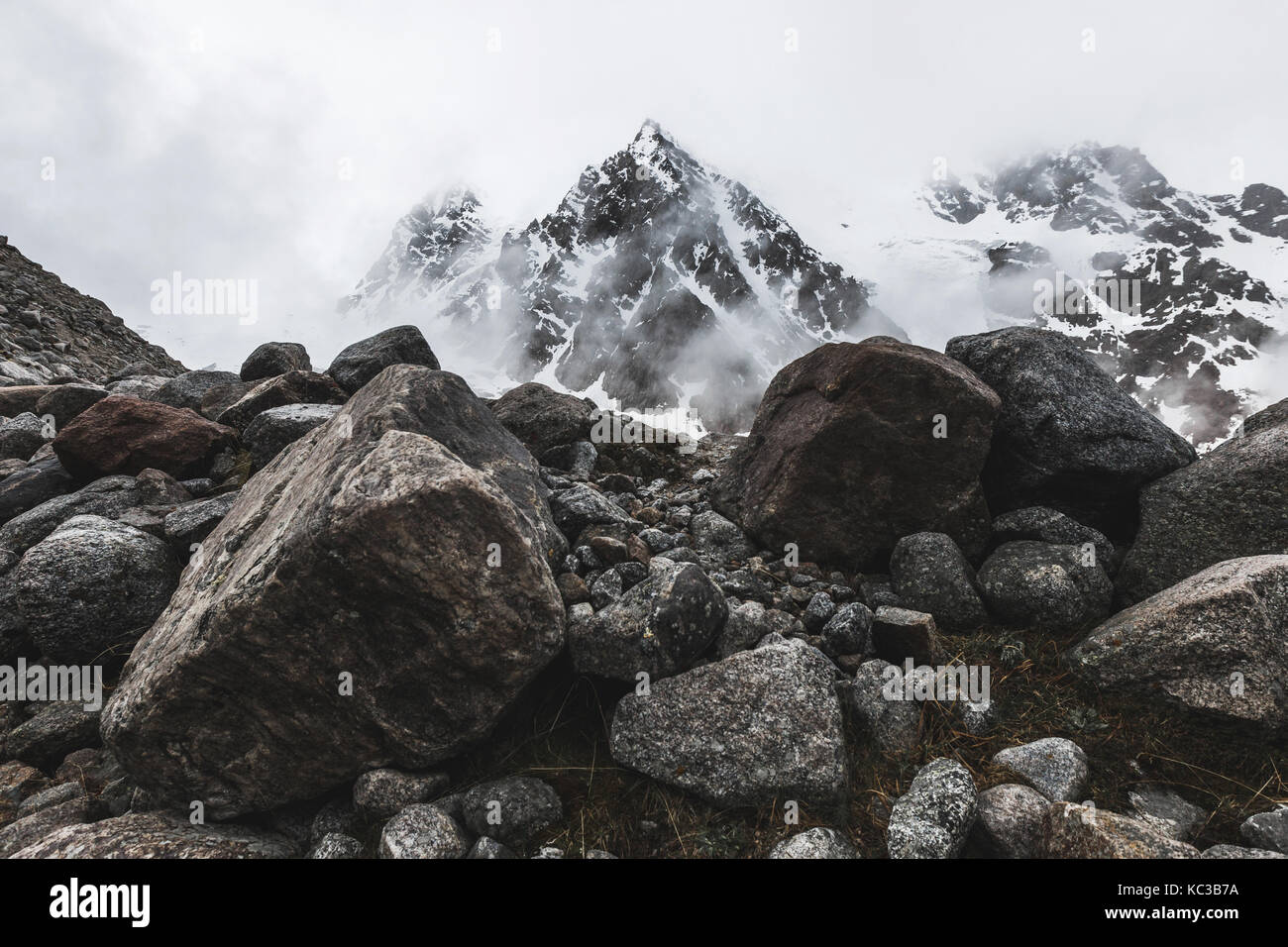 Mountain landscape with rocks and creeping fog. High snow peaks in the ...
